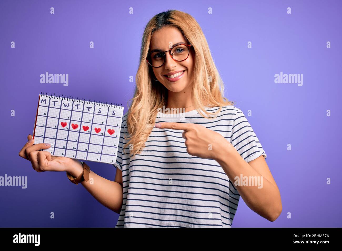 Young beautiful blonde woman holding period calendar to control ...