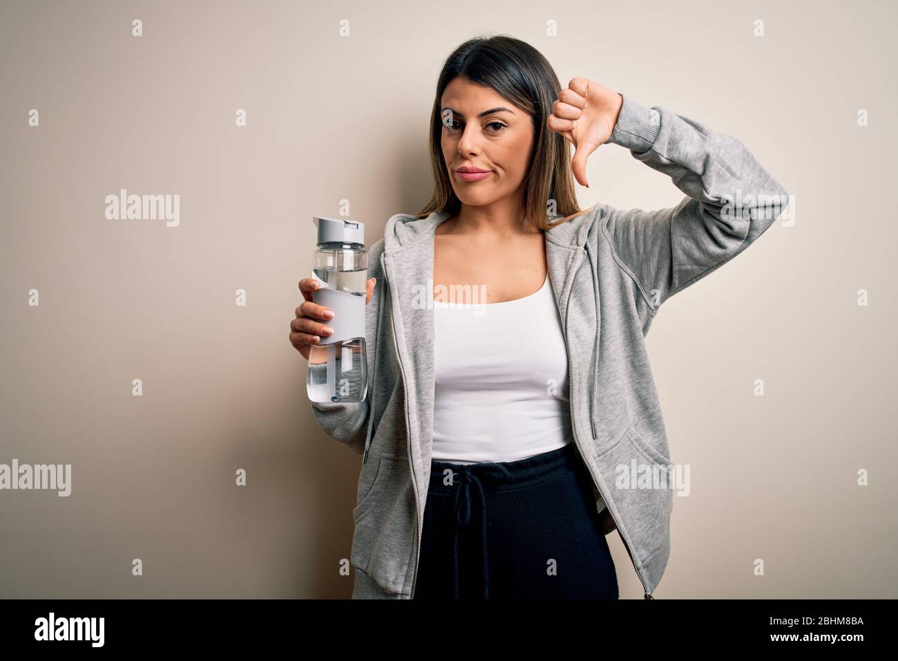 Young beautiful brunette sporty woman drinking bottle of water over ...
