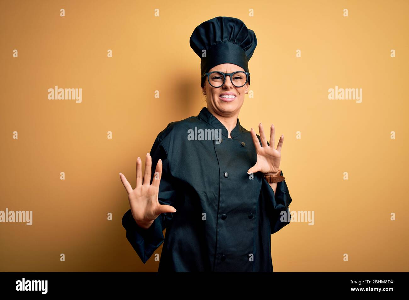 Young beautiful brunette chef woman wearing cooker uniform and hat over ...
