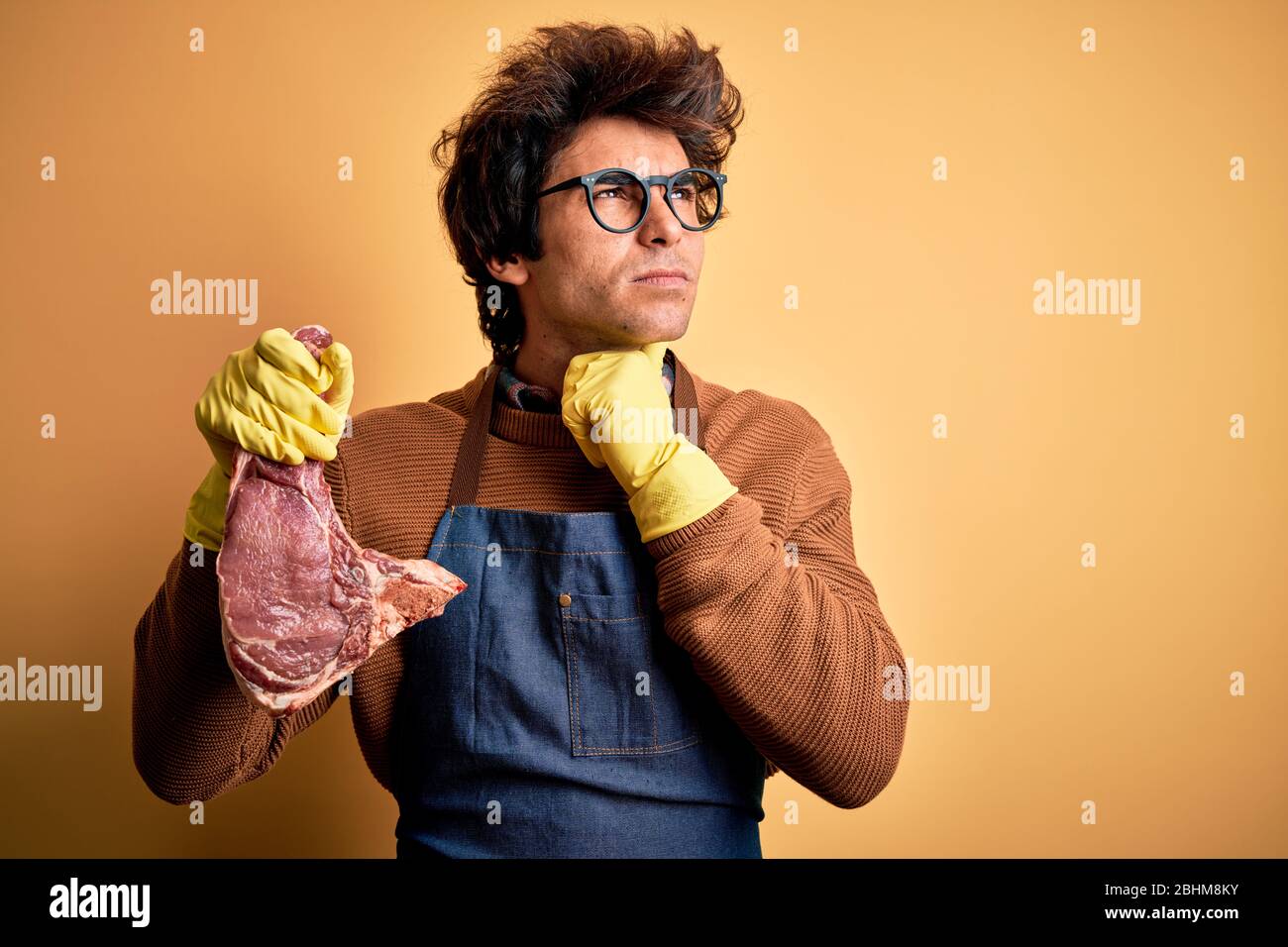 Young handsome butcher man holding meet steak standing over isolated ...