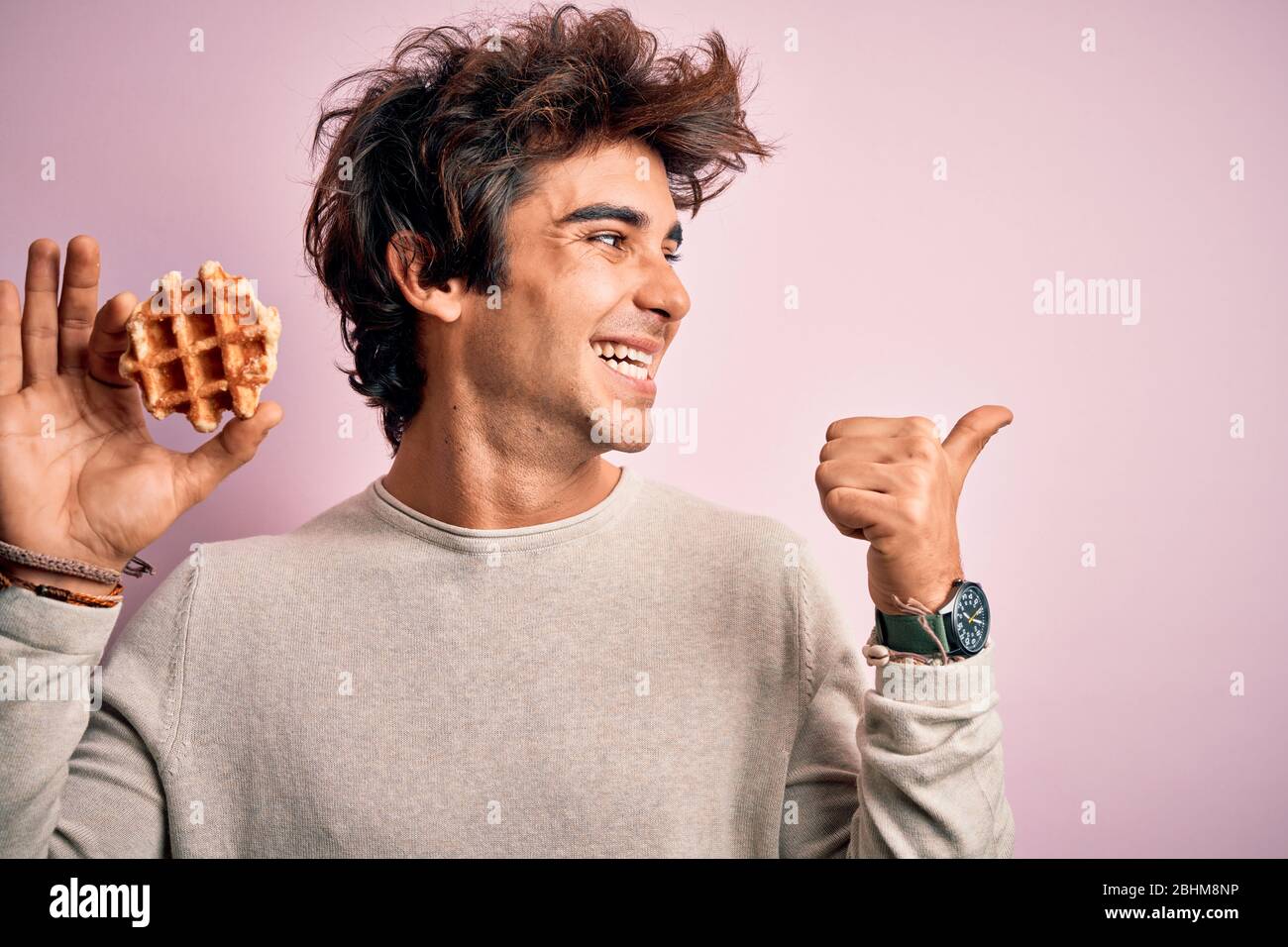 Young handsome man holding sweet waffle standing over isolated pink ...