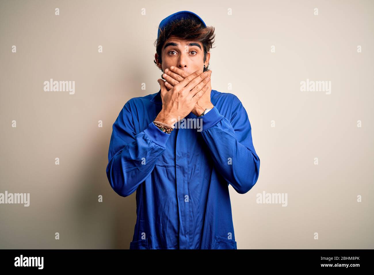 Young mechanic man wearing blue cap and uniform standing over isolated ...