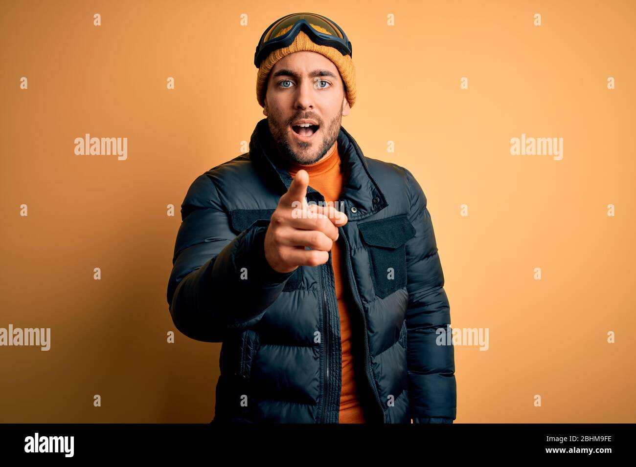 Young handsome skier man with beard wearing snow sportswear and ski ...