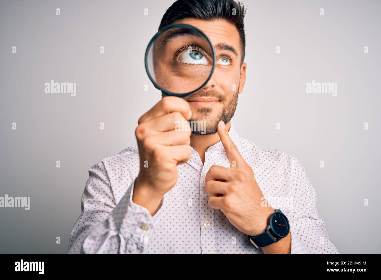 Young detective man looking through magnifying glass over isolated ...