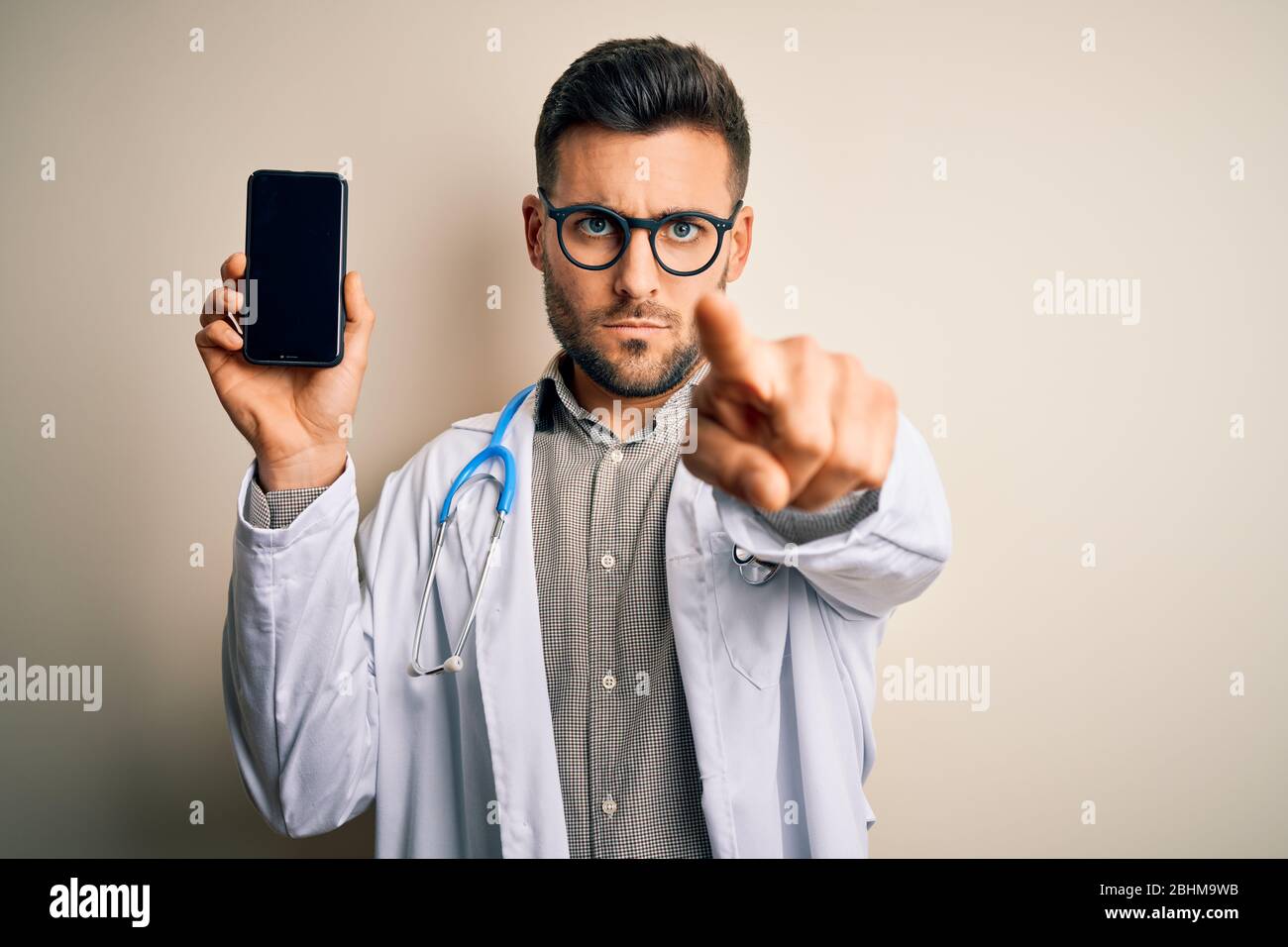 Young doctor man wearing stethoscope showing smartphone screen over ...