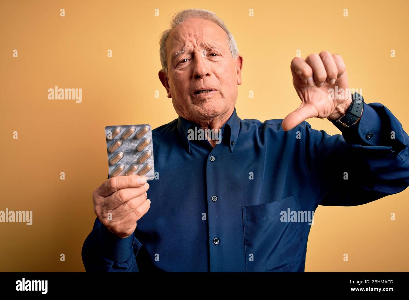 Senior grey haired man holding pharmaceutical pill drugs over yellow ...