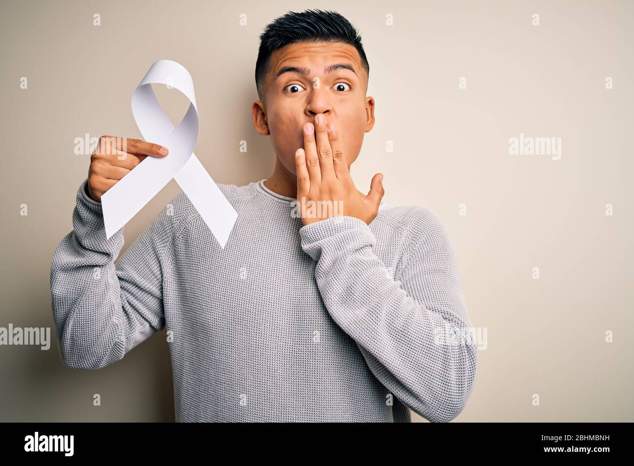 Young latin man holding white cancer ribbon supporting stop women ...