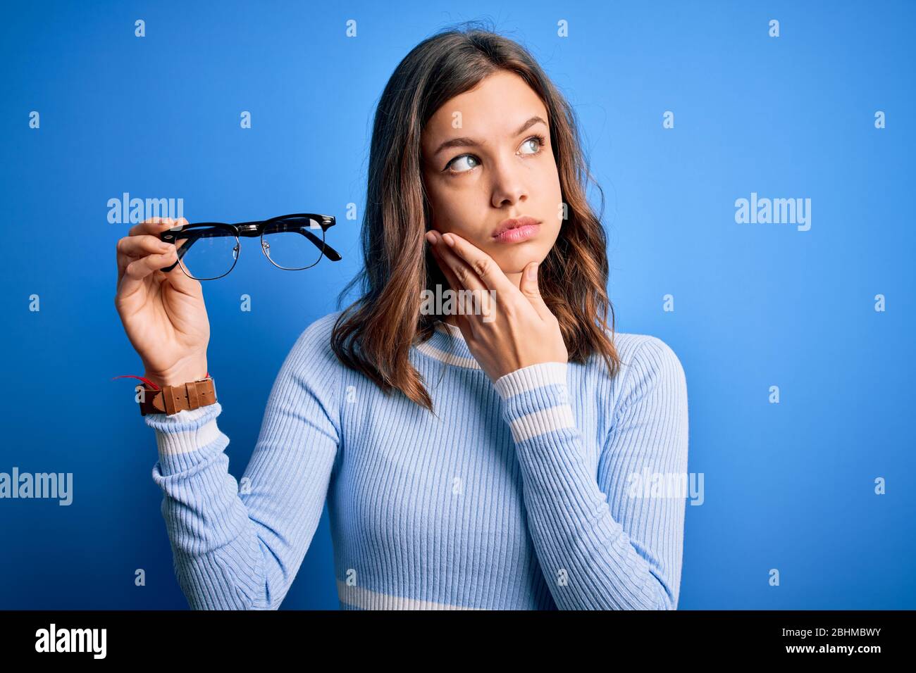 Young blonde girl holding eyeglasses optical lens over blue isolated ...