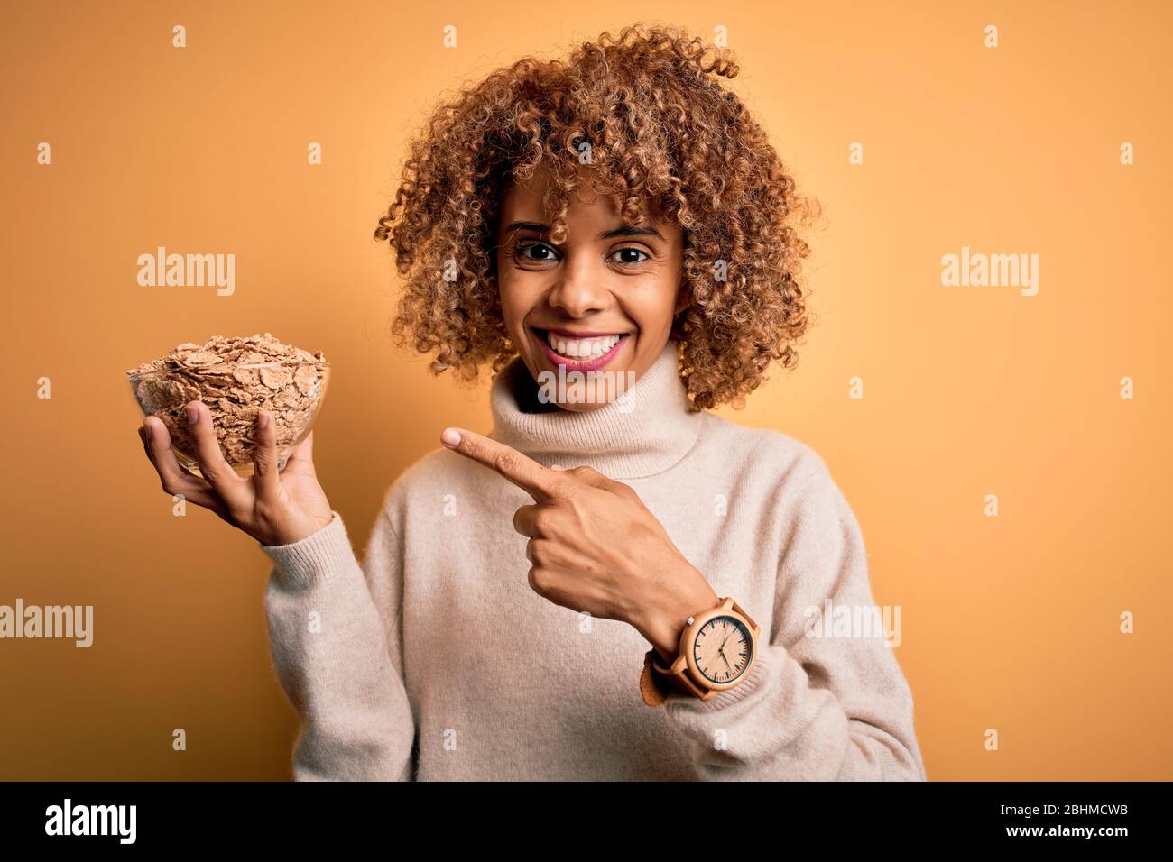 Young african american curly woman holding bowl with healthy cornflakes ...