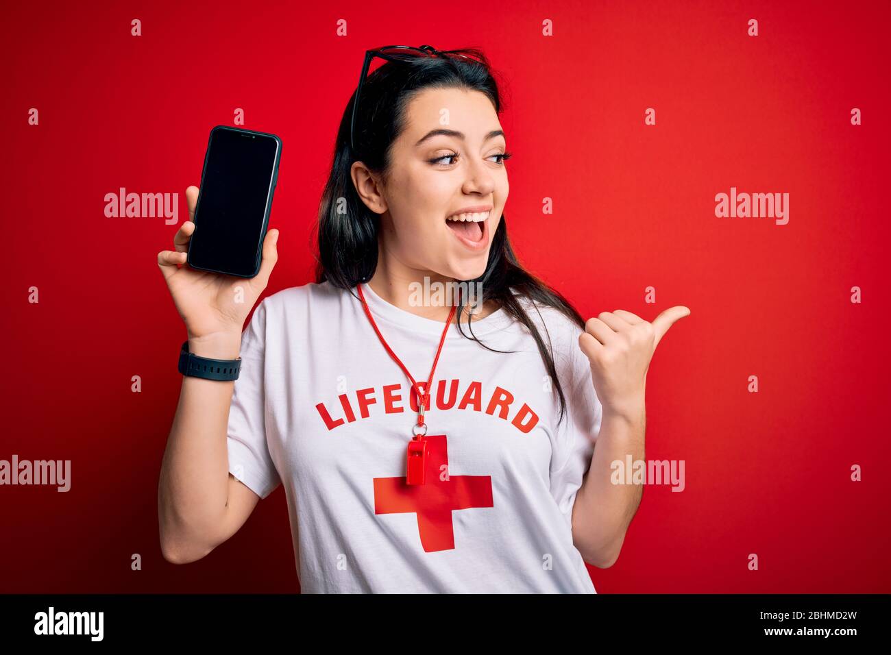 Young lifeguard woman showing smartphone screen over red background ...