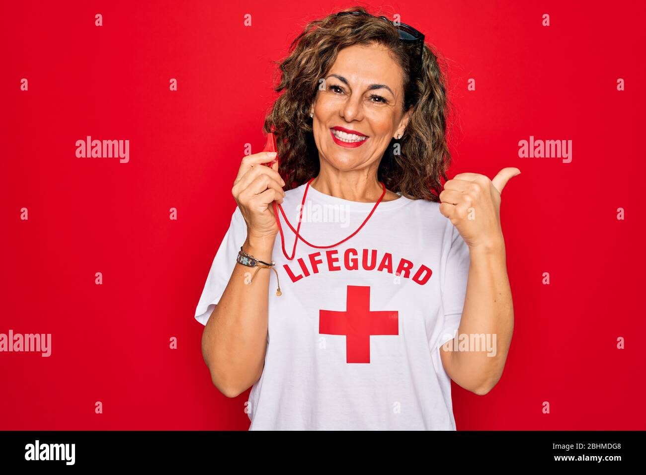 Middle age senior summer lifeguard woman holding whistle over red ...
