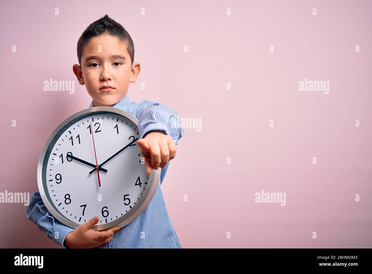 Young little boy kid holding big minute clock over isolated pink ...