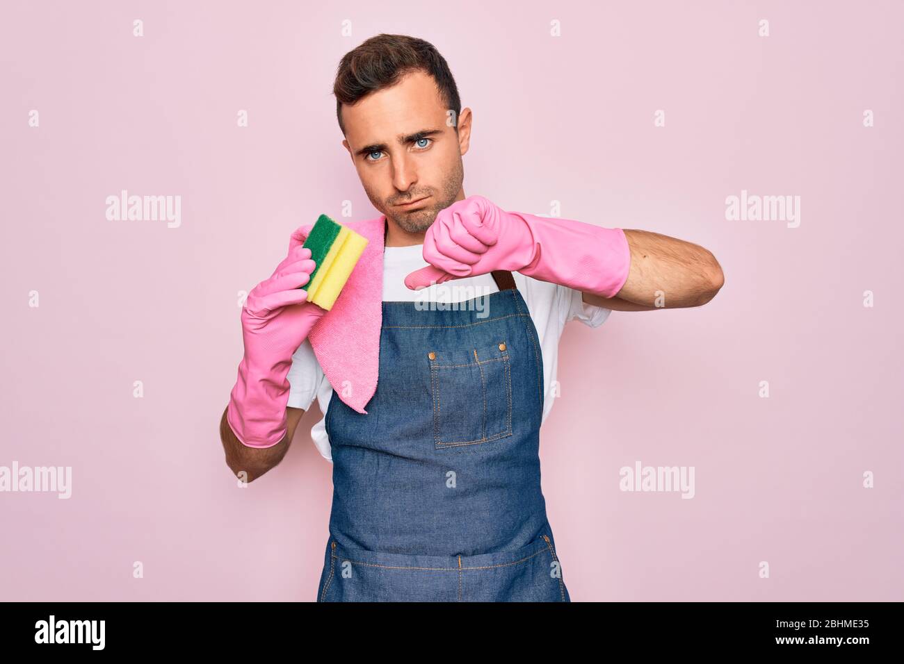 Young cleaner man with blue eyes cleaning wearing apron and gloves ...
