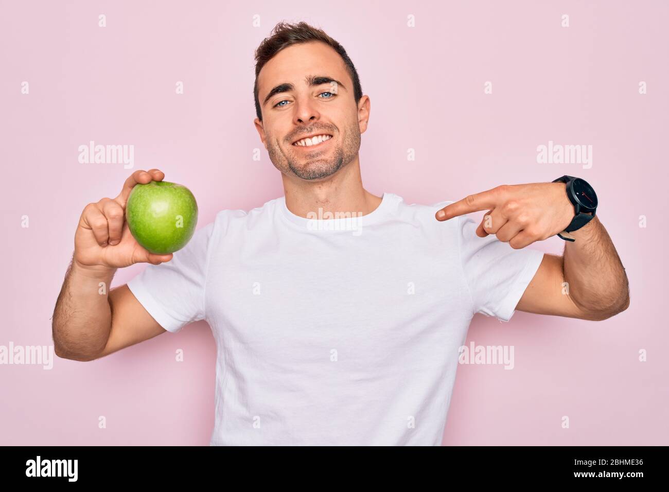 Young handsome man with blue eyes eating healthy green apple over ...