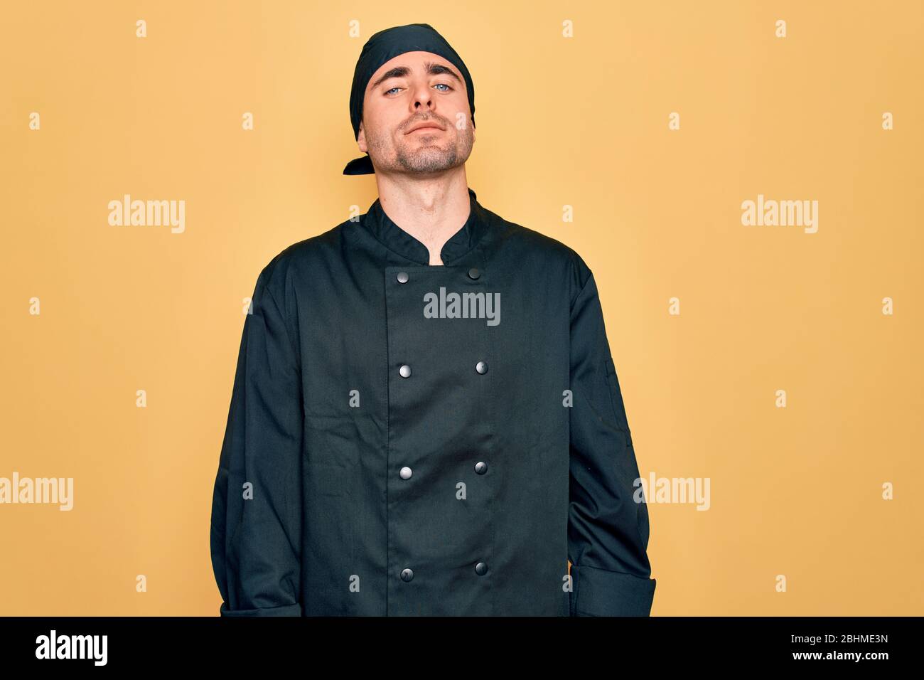 Young handsome cooker man with blue eyes wearing uniform and hat over ...