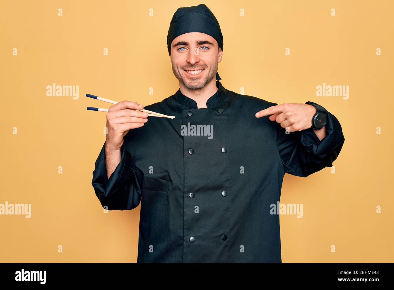 Young handsome cooker man with blue eyes wearing uniform and hat using ...