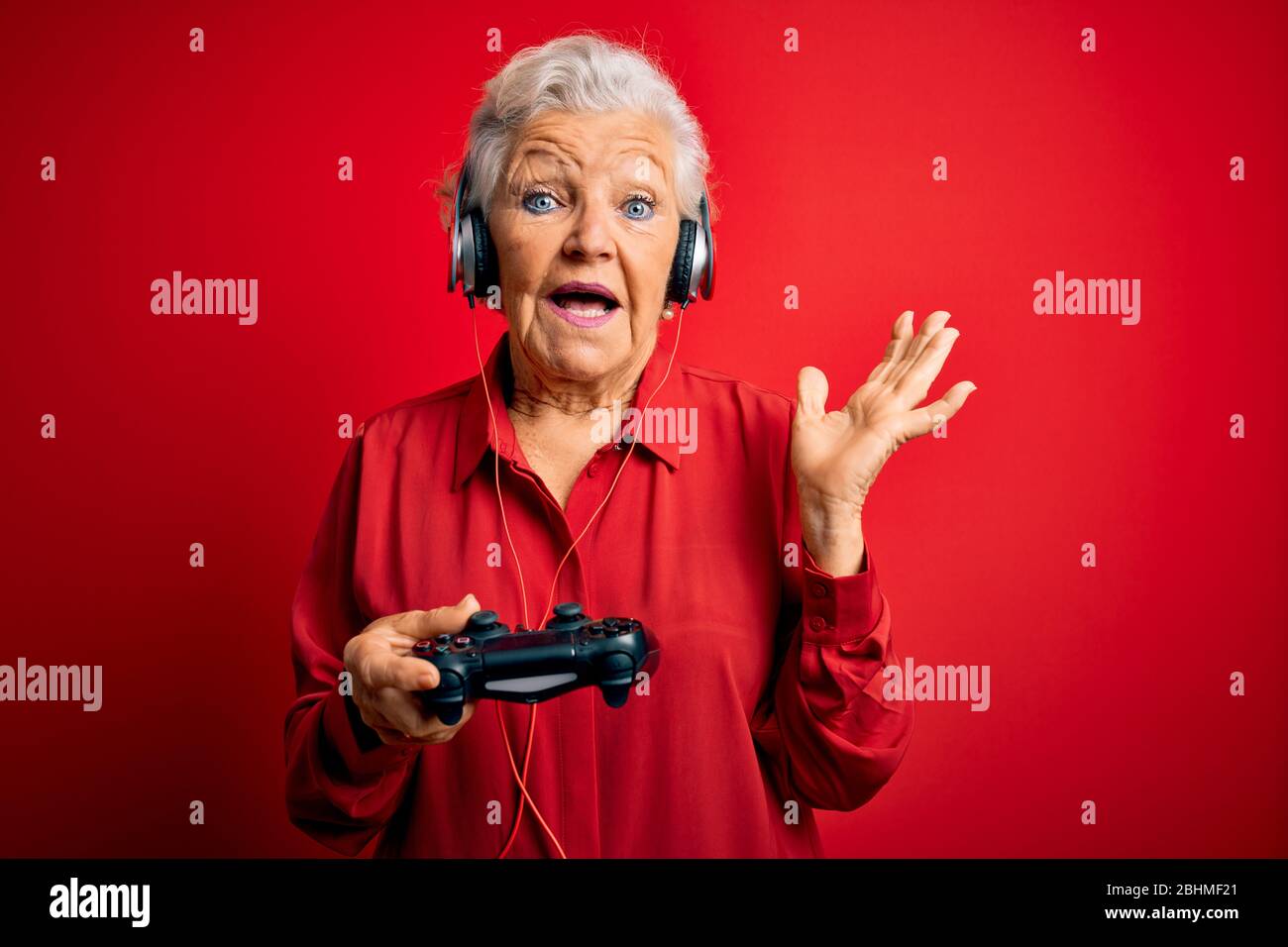 Senior beautiful grey-haired gamer woman playing video game using ...