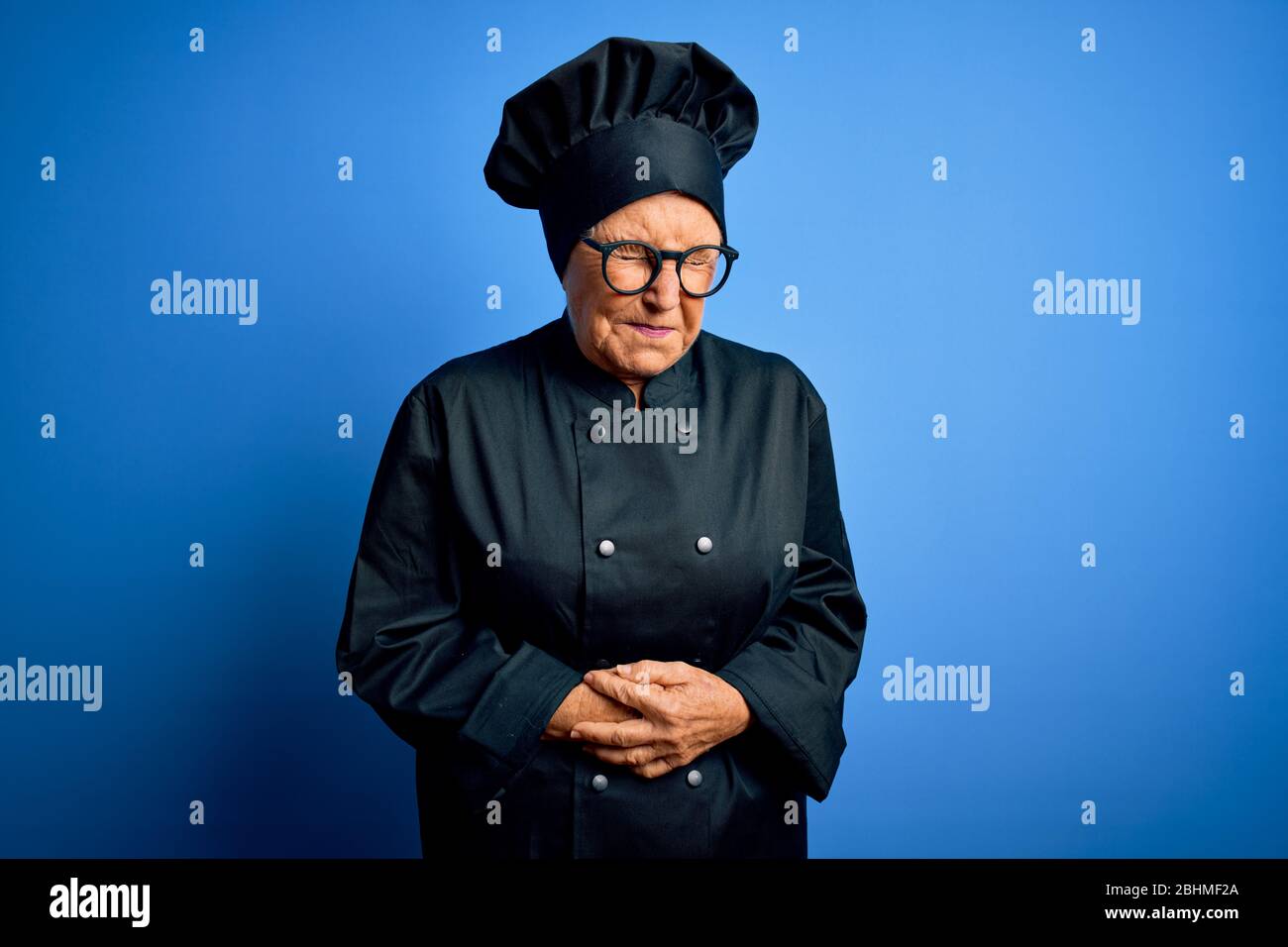 Senior beautiful grey-haired chef woman wearing cooker uniform and hat ...