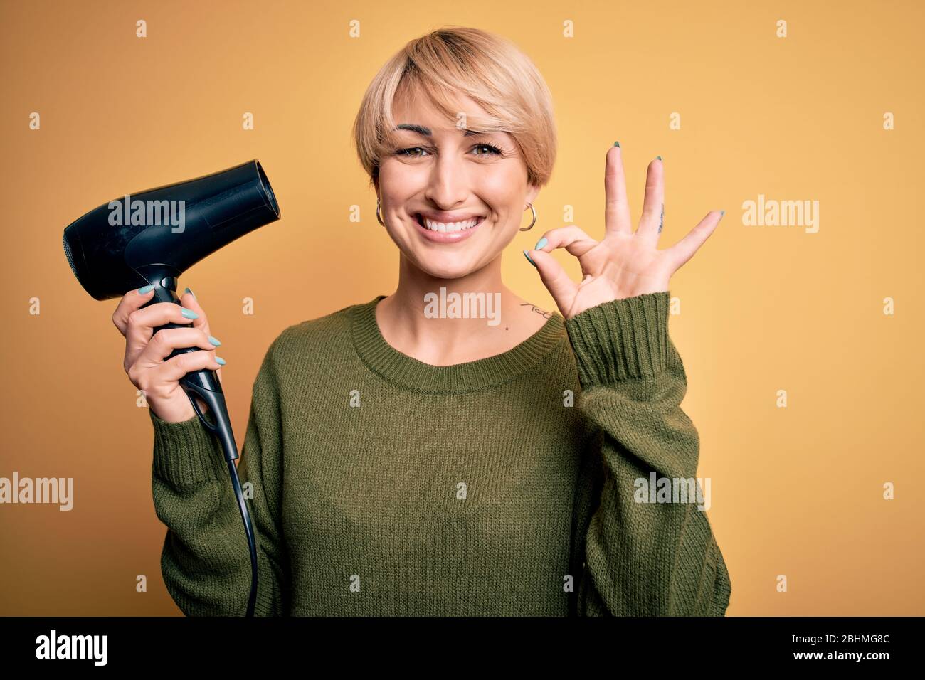 Young blonde woman with short hair drying her hair using hairdryer over ...