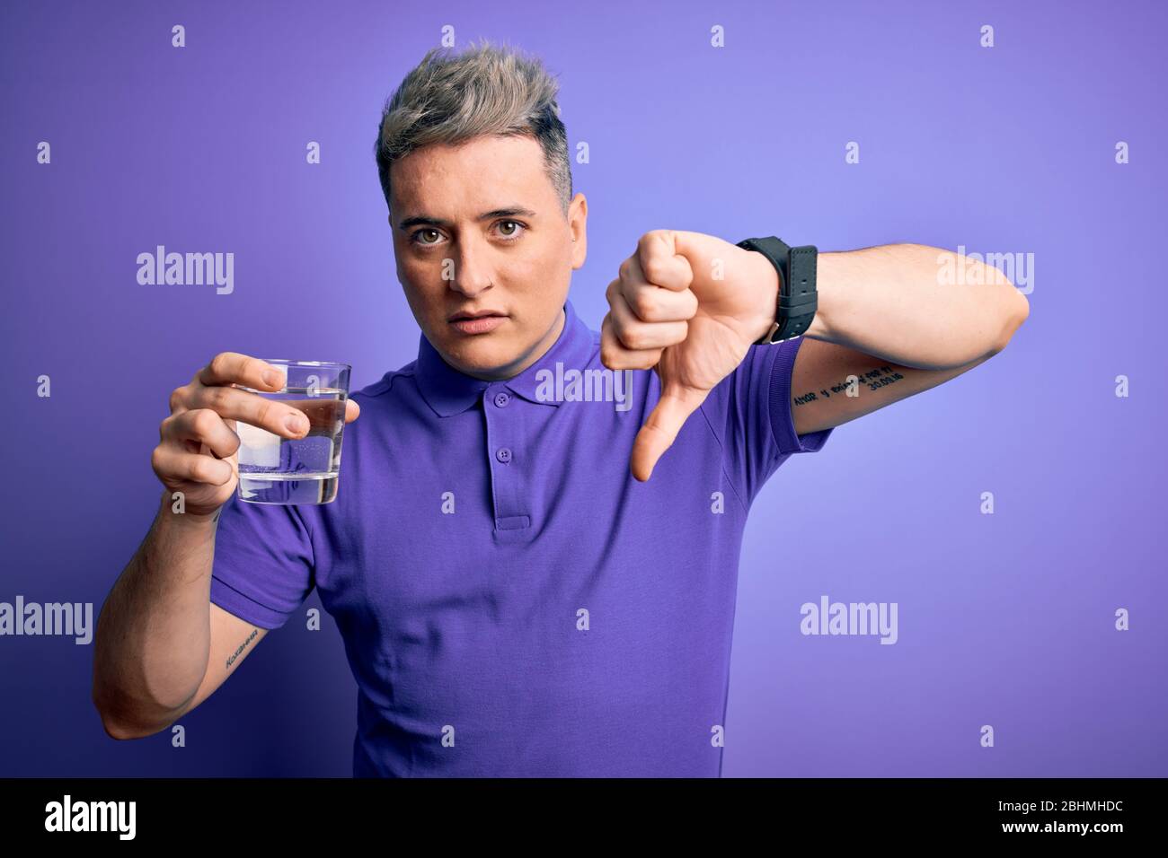 Young modern man drinking a glass of fresh water over purple isolated ...