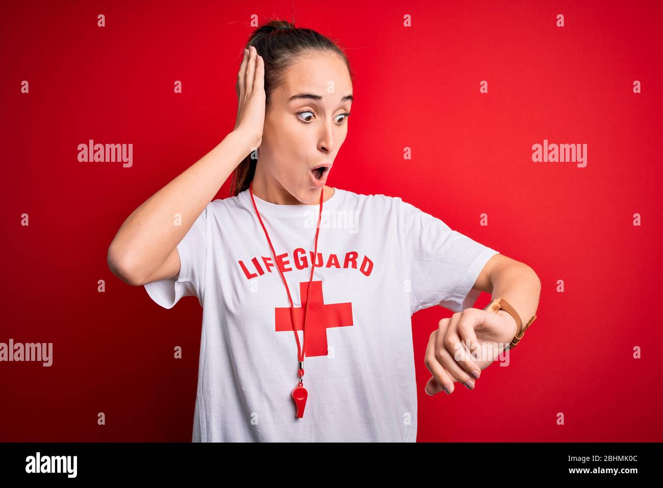 Beautiful lifeguard woman wearing t-shirt with red cross using whistle ...