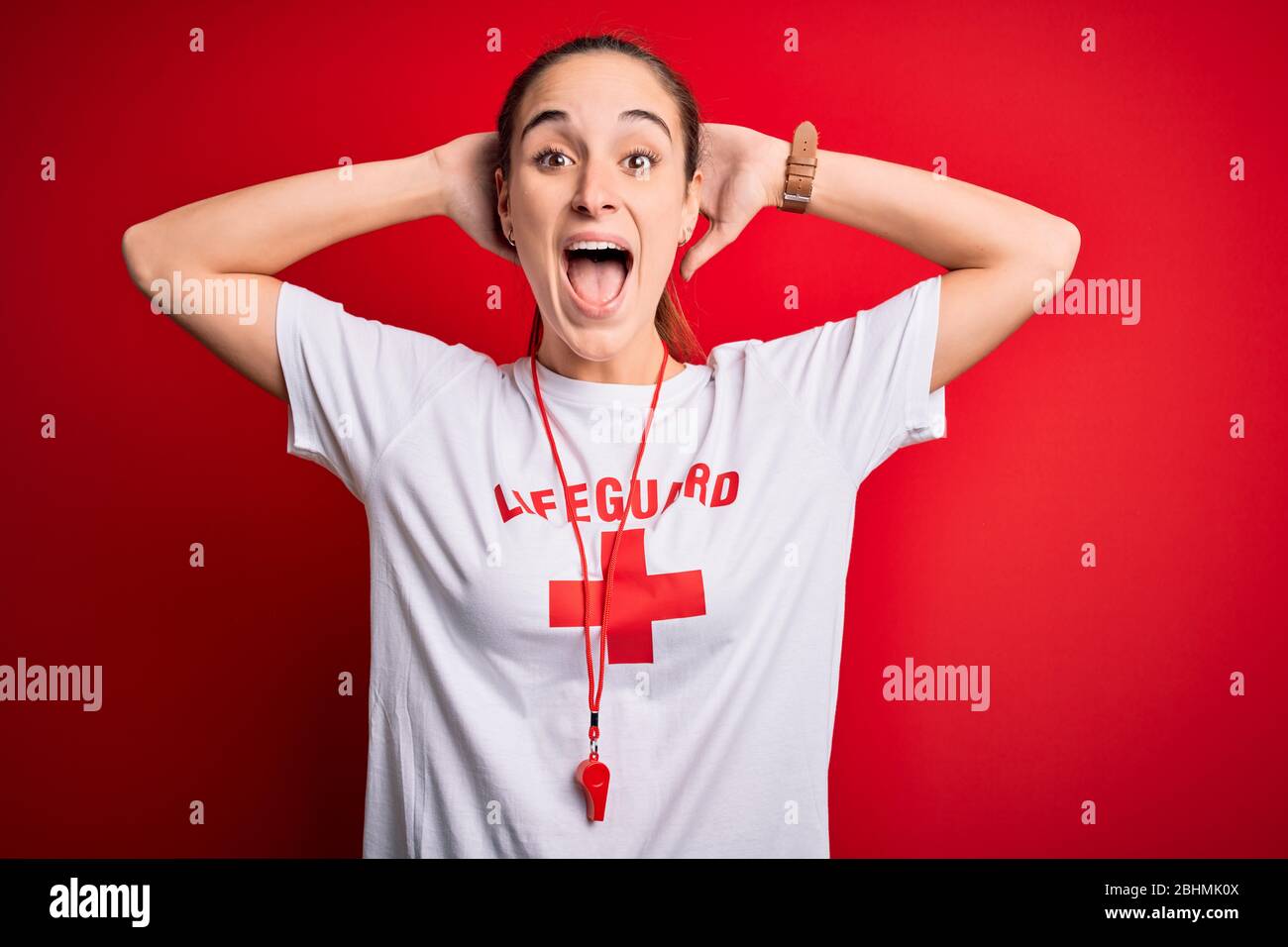 Beautiful lifeguard woman wearing t-shirt with red cross using whistle ...