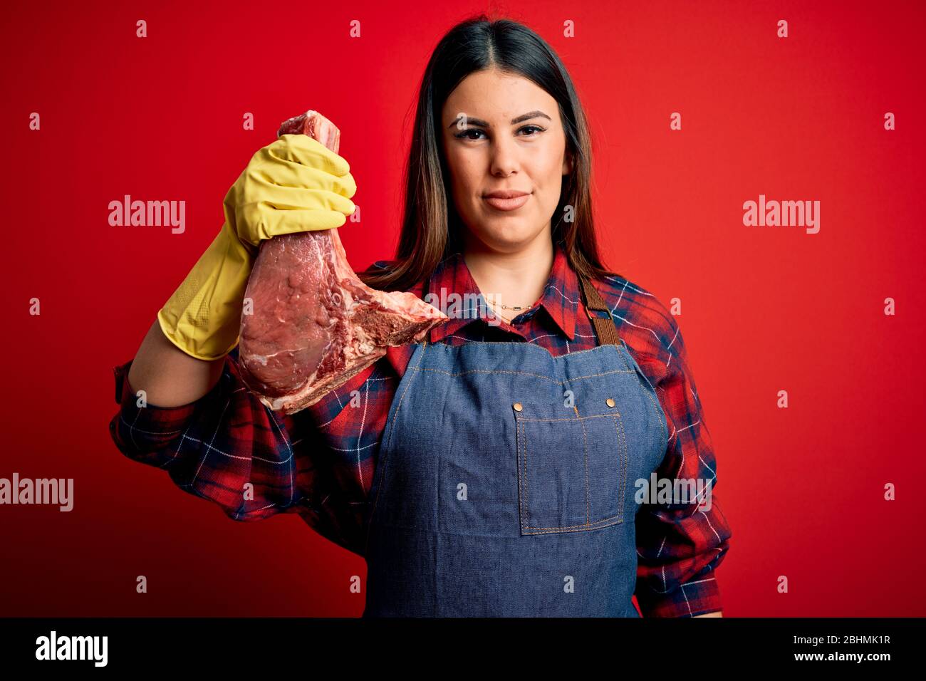Young butcher woman holding fresh raw beef meat stake over red ...