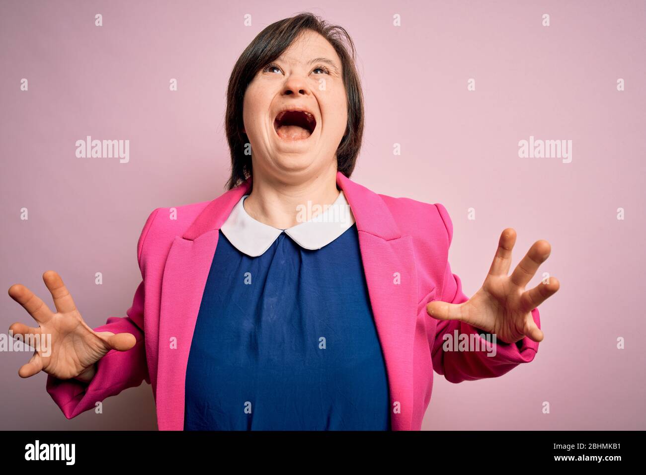 Young down syndrome business woman over pink background crazy and mad ...