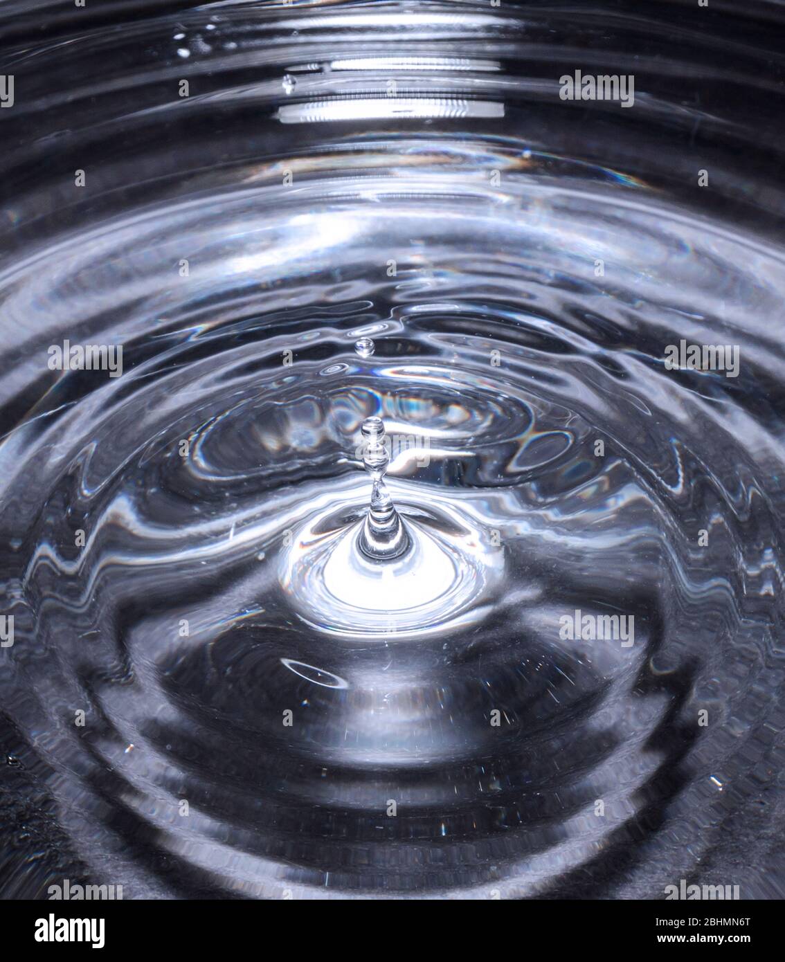 Closeup water drop dripping from the top to the surface of pure water ...