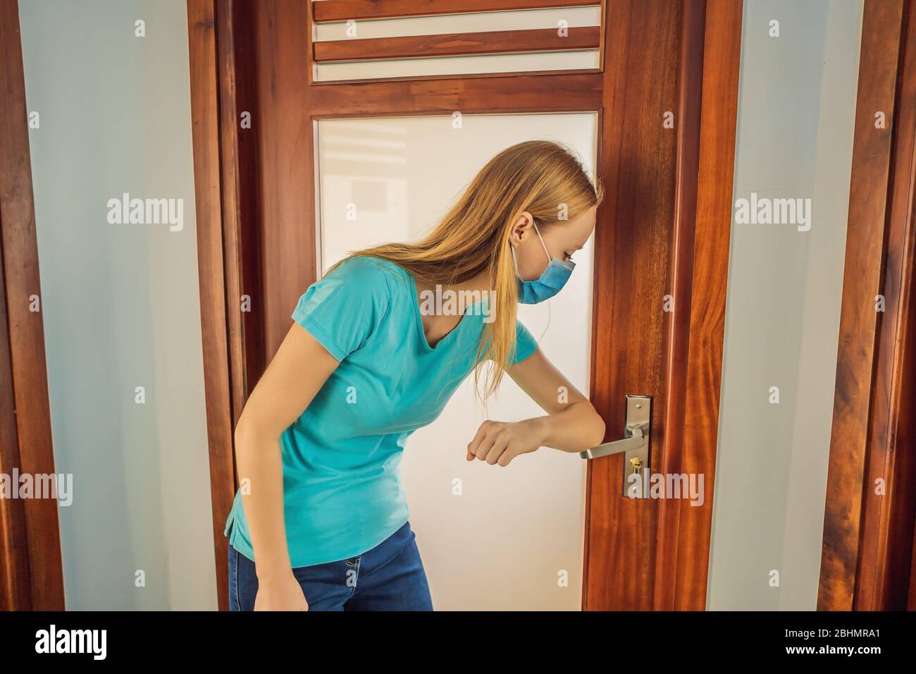 Woman wearing mask opening the door with the elbow for protection ...