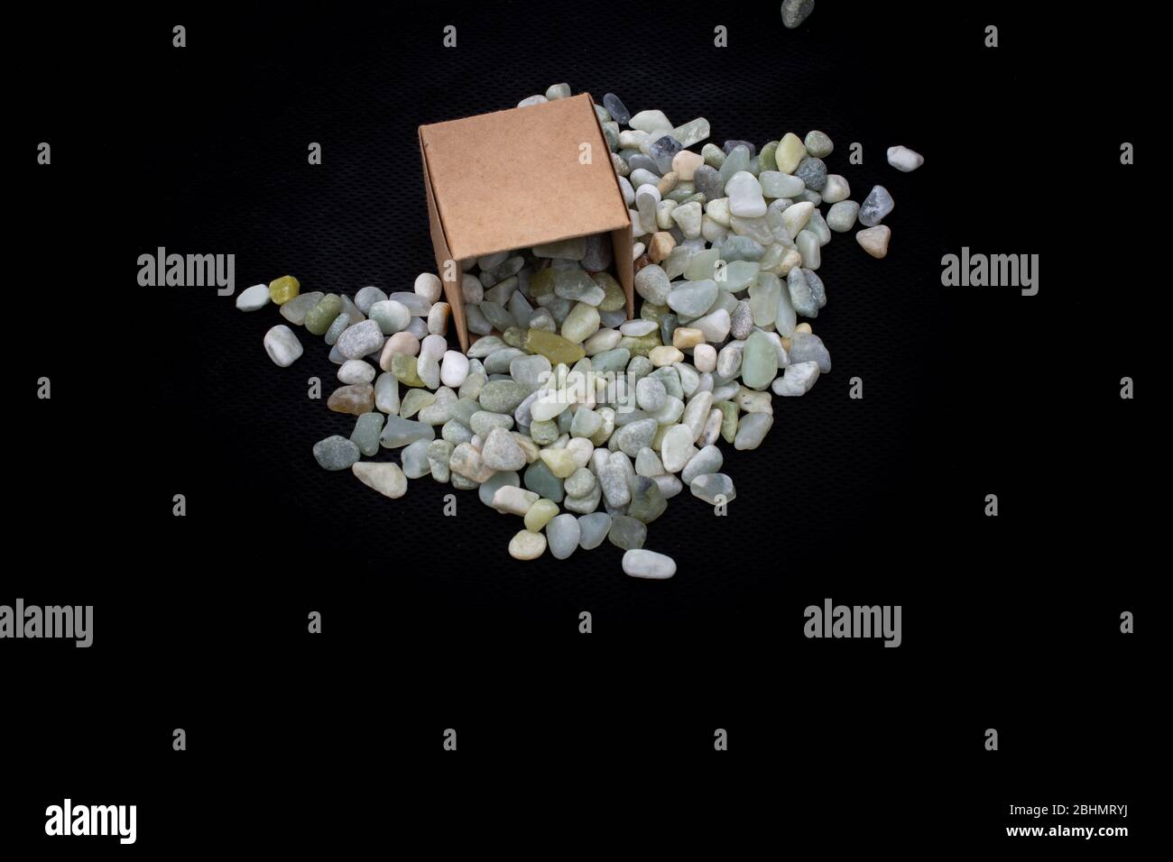 Stone pebbles gravels around brown cardboard box on a black background ...