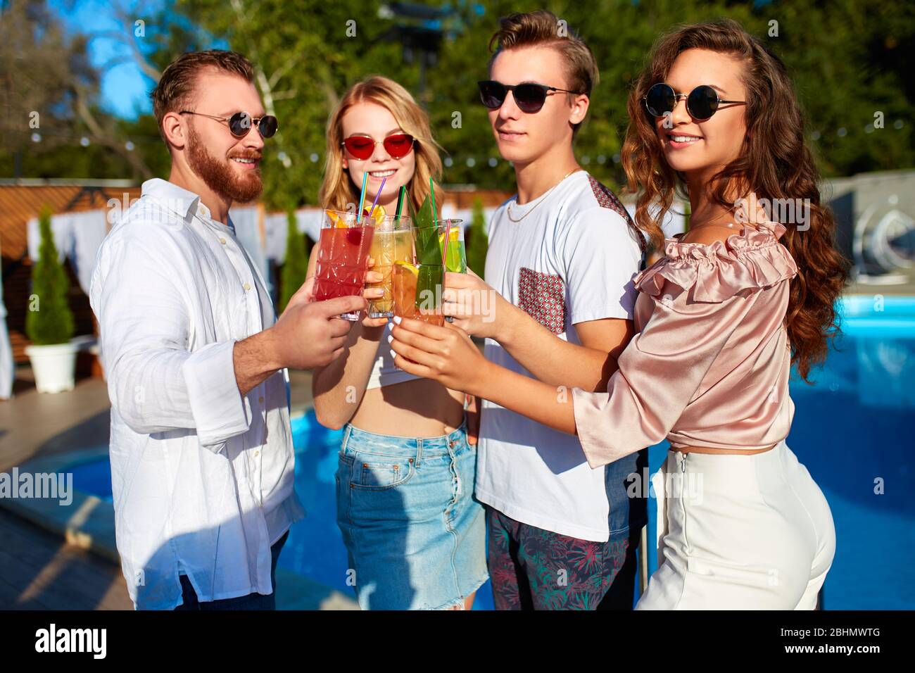Group of friends having fun at poolside summer party, clinking glasses ...