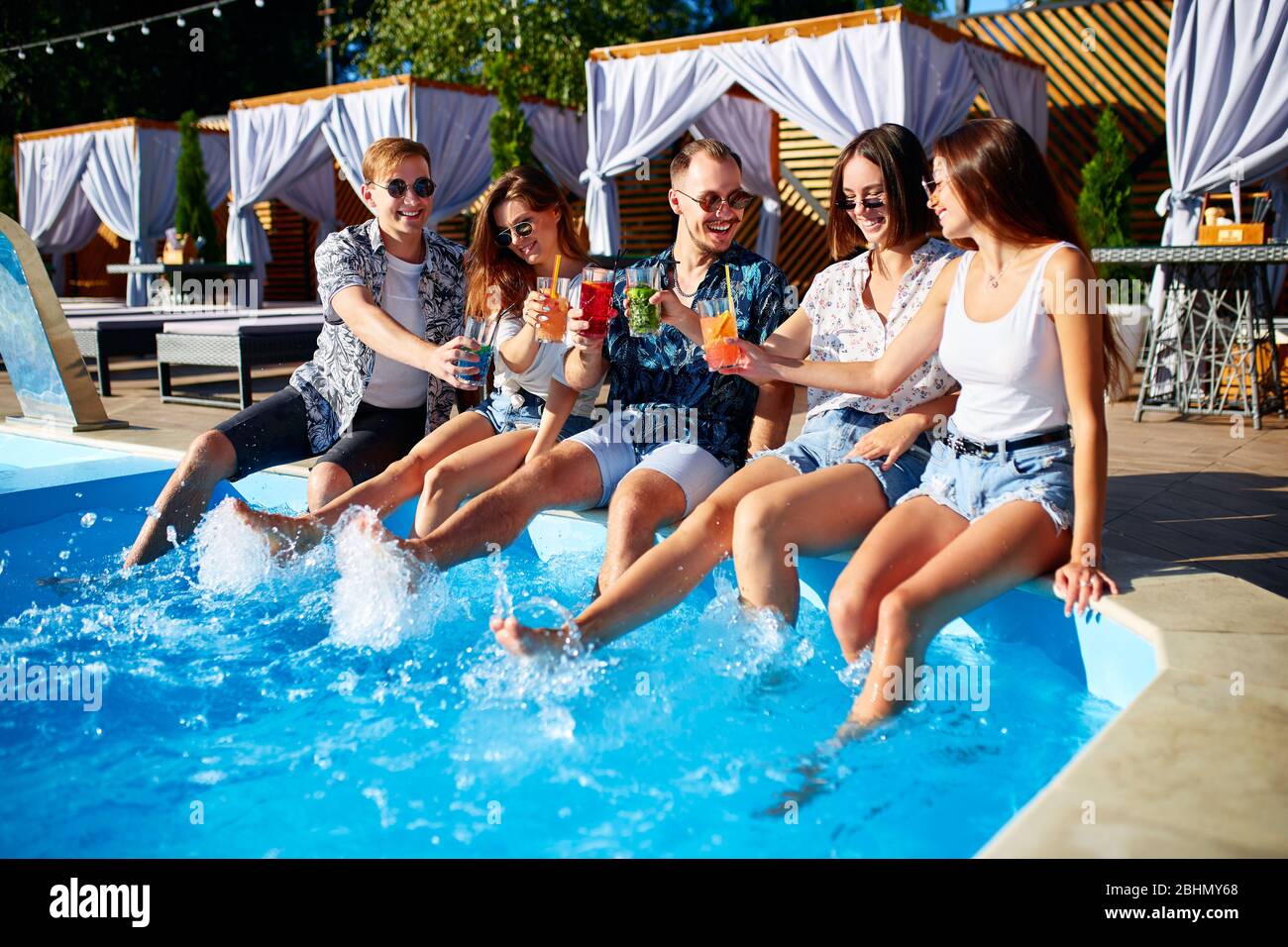 Group of friends having fun at poolside party clinking glasses with ...