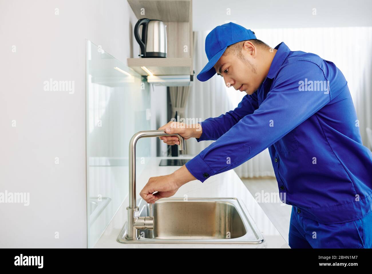 Repairman in cap and uniform fixing water tap in kitchen sink Stock ...