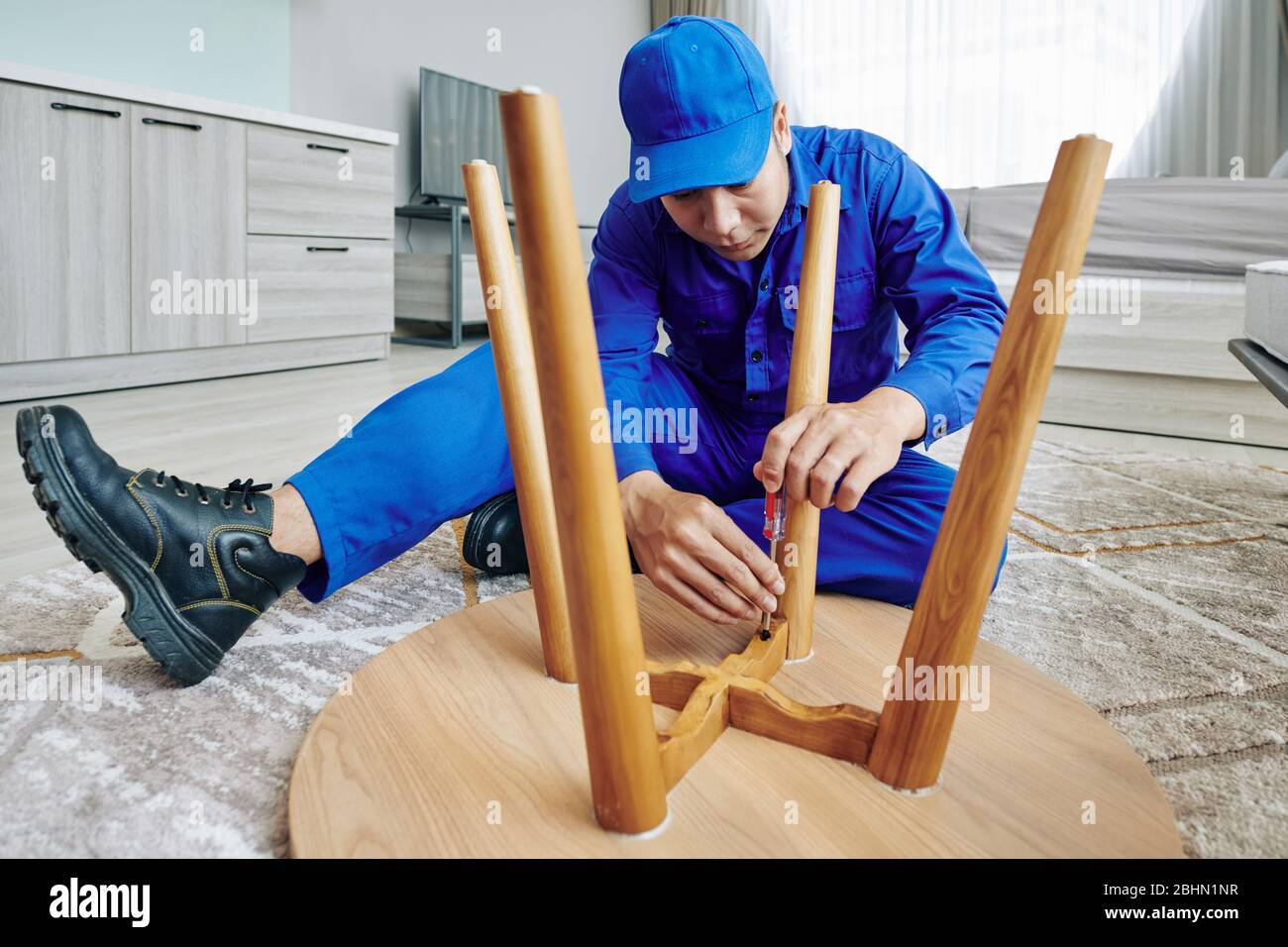Handyman using screwdriver when assembling wooden table in apartment of ...