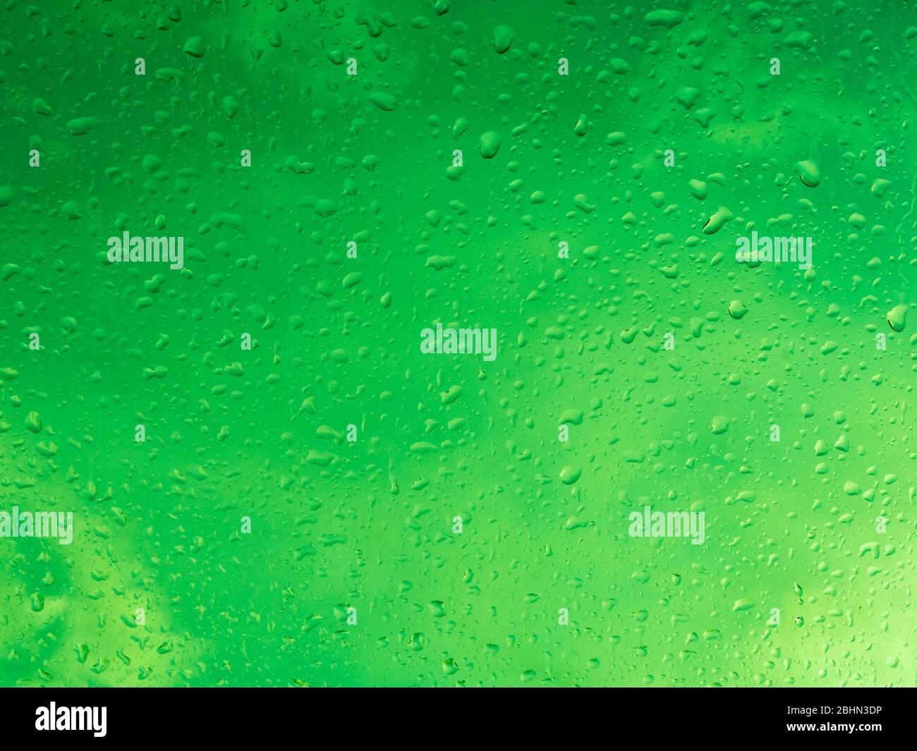 Wet green window with rain drops and a cloudy sky outside background ...