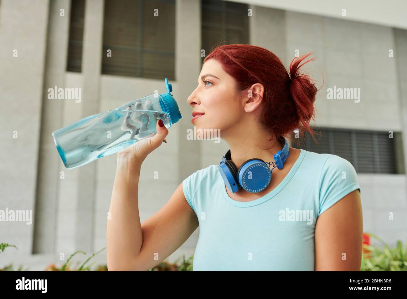 Beautiful young woman with headphones on her neck drinking fresh water ...