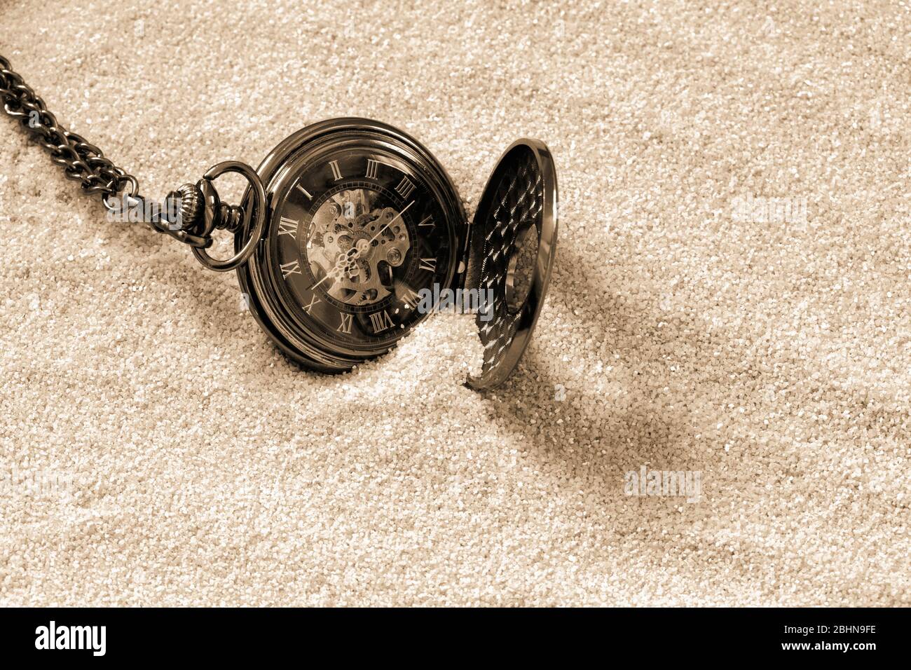 Antique old pocket fob watch with chain partly buried in sand. With ...