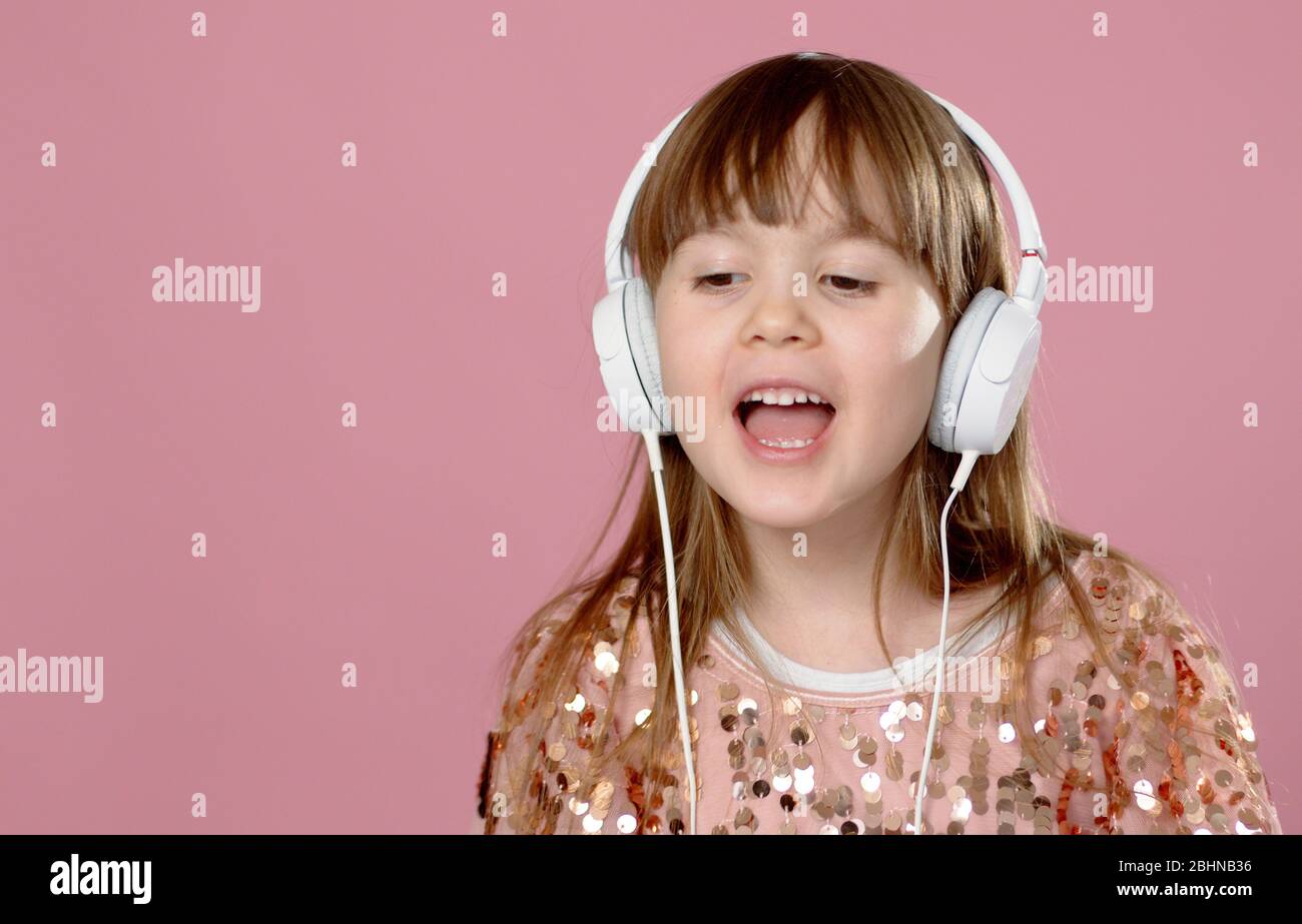 Pretty 6 or 7 years old little girl singing and dancing with headphones ...