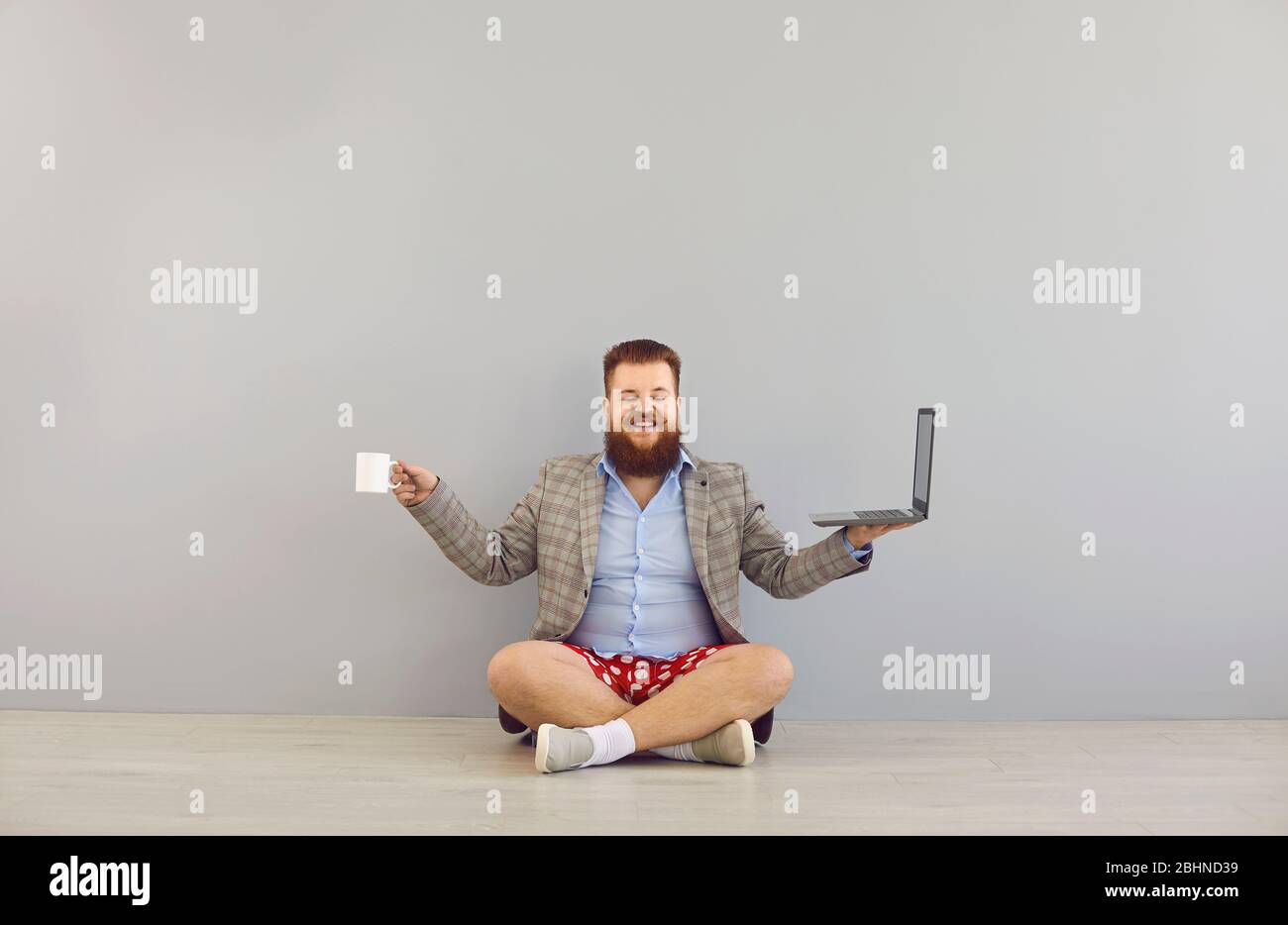 Funny fat bearded man in a jacket and red shorts with a laptop on a ...