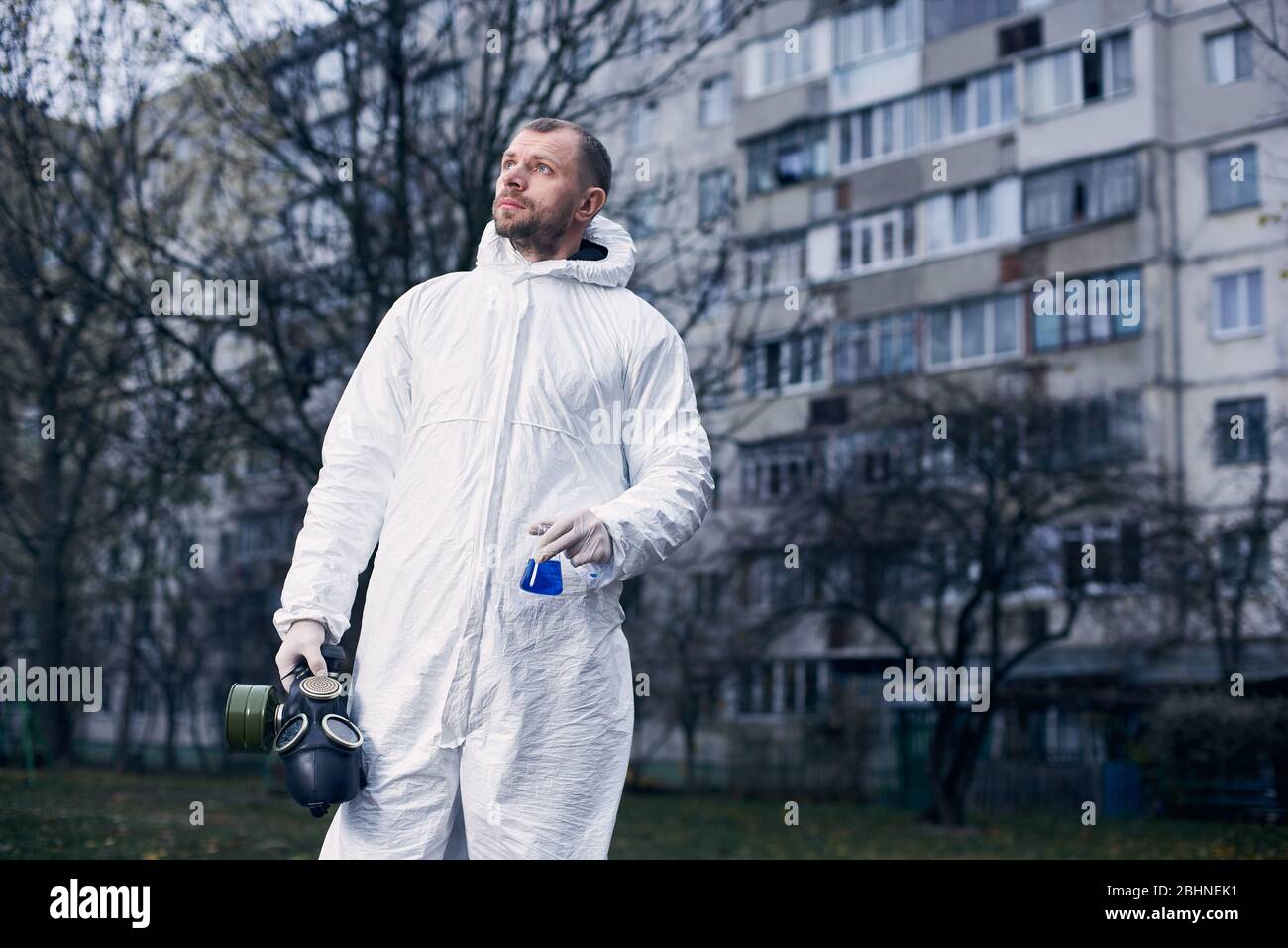 Male ecologist in white coverall, holding gas mask in one hand and ...