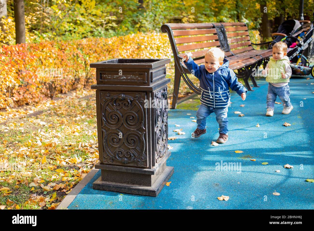 A little cute baby in blue clothes goes to a street bin in a park and ...
