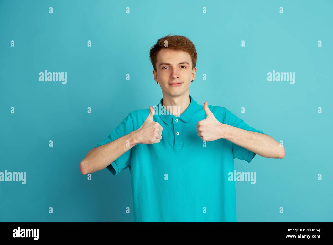 Thumbs up. Caucasian young man's modern portrait isolated on blue ...