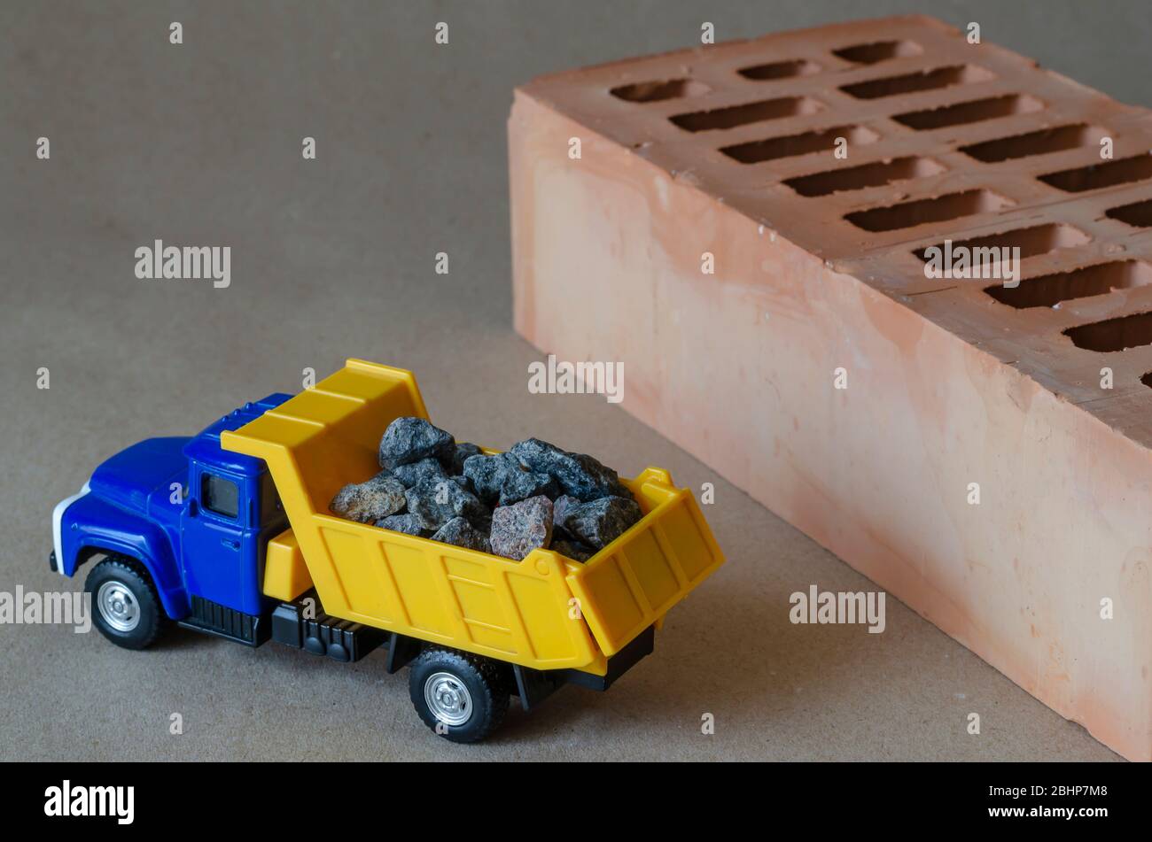 A yellow dump truck carries rubble next to a brick. Toy truck with a ...