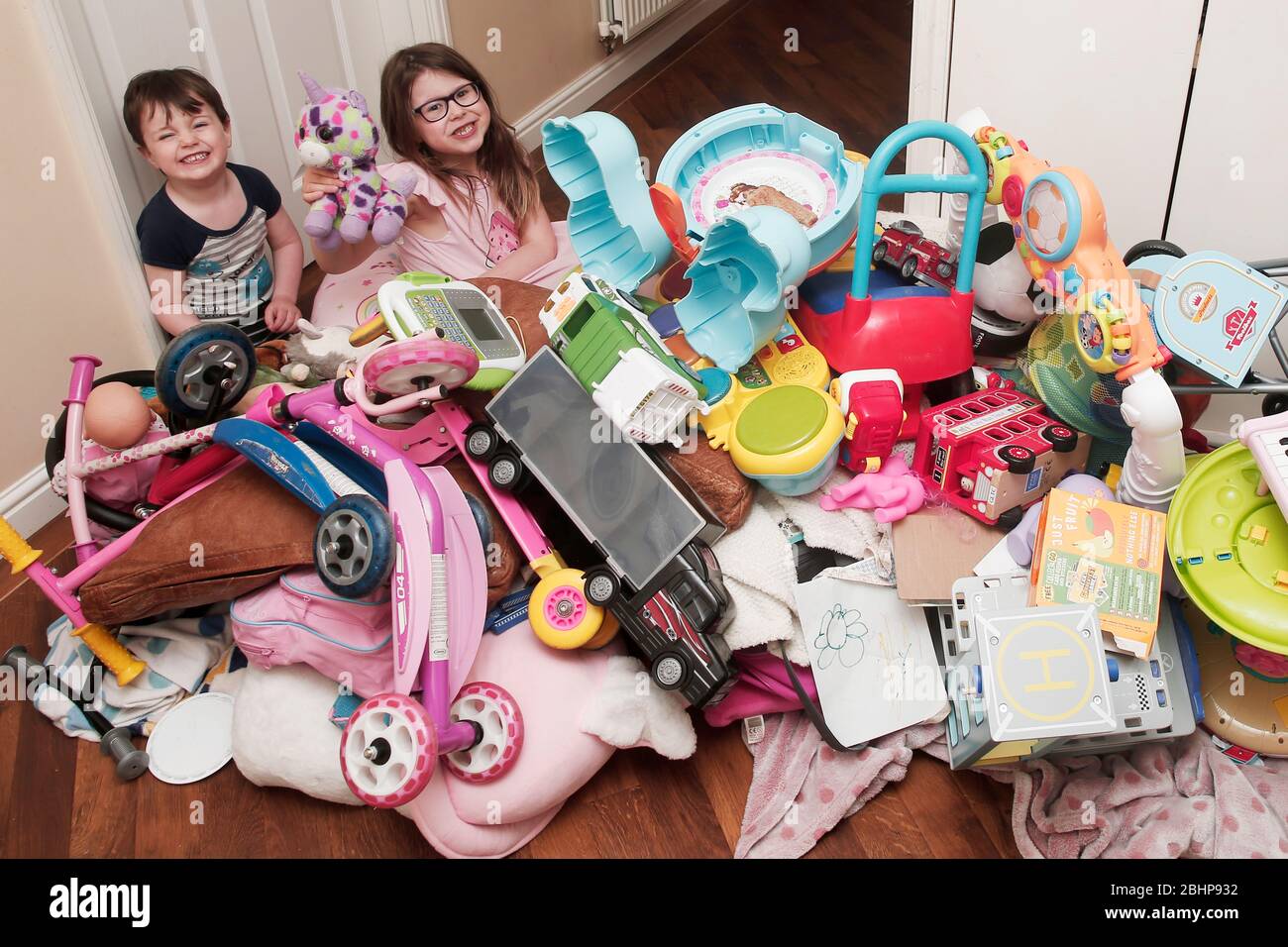Two siblings surrounded by huge pile of children's toys at home Stock ...