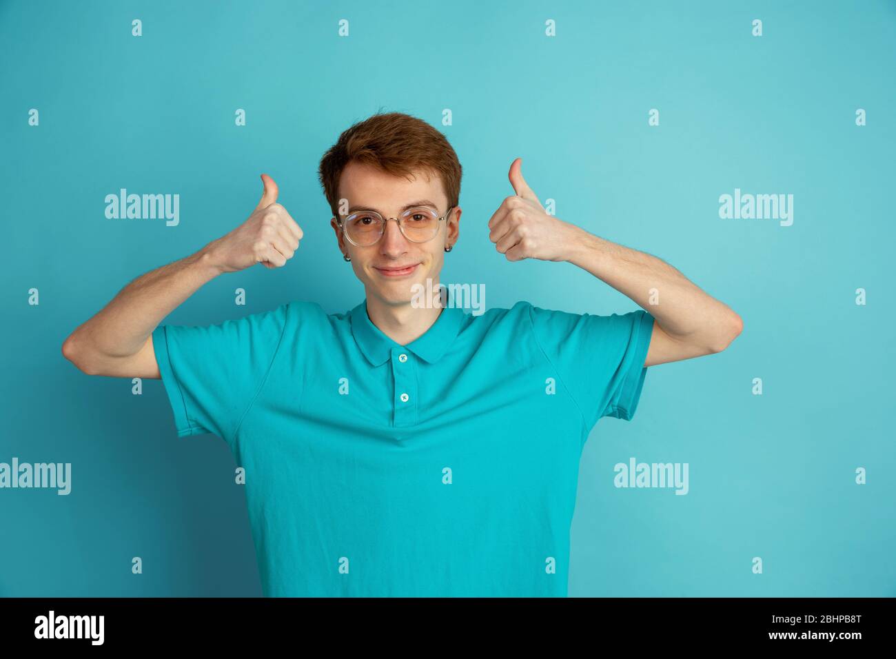 Thumbs up. Caucasian young man's modern portrait isolated on blue ...