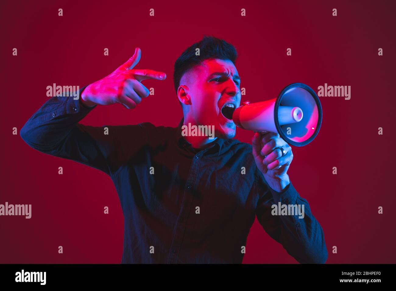Shouting with speaker. Caucasian young man's portrait isolated on red ...