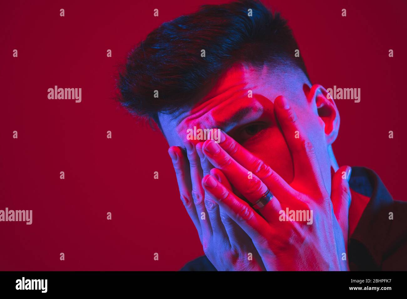 Hiding face with hands. Caucasian young man's portrait isolated on red ...