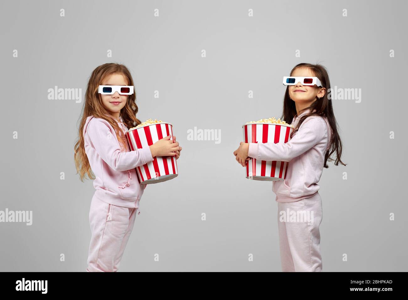 two beautiful caucasian smiling little girls in red-blue 3d glasses holding popcorn buckets and ...