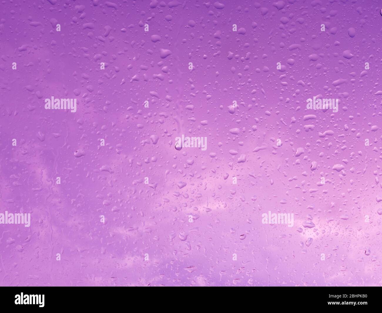 Wet pink window with rain drops and a cloudy sky outside background ...